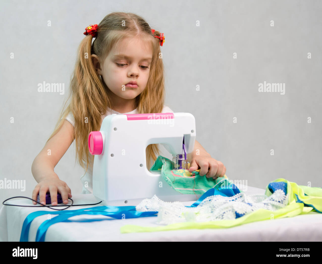Girl sew on a children's sewing machine. Studio, a white background ...