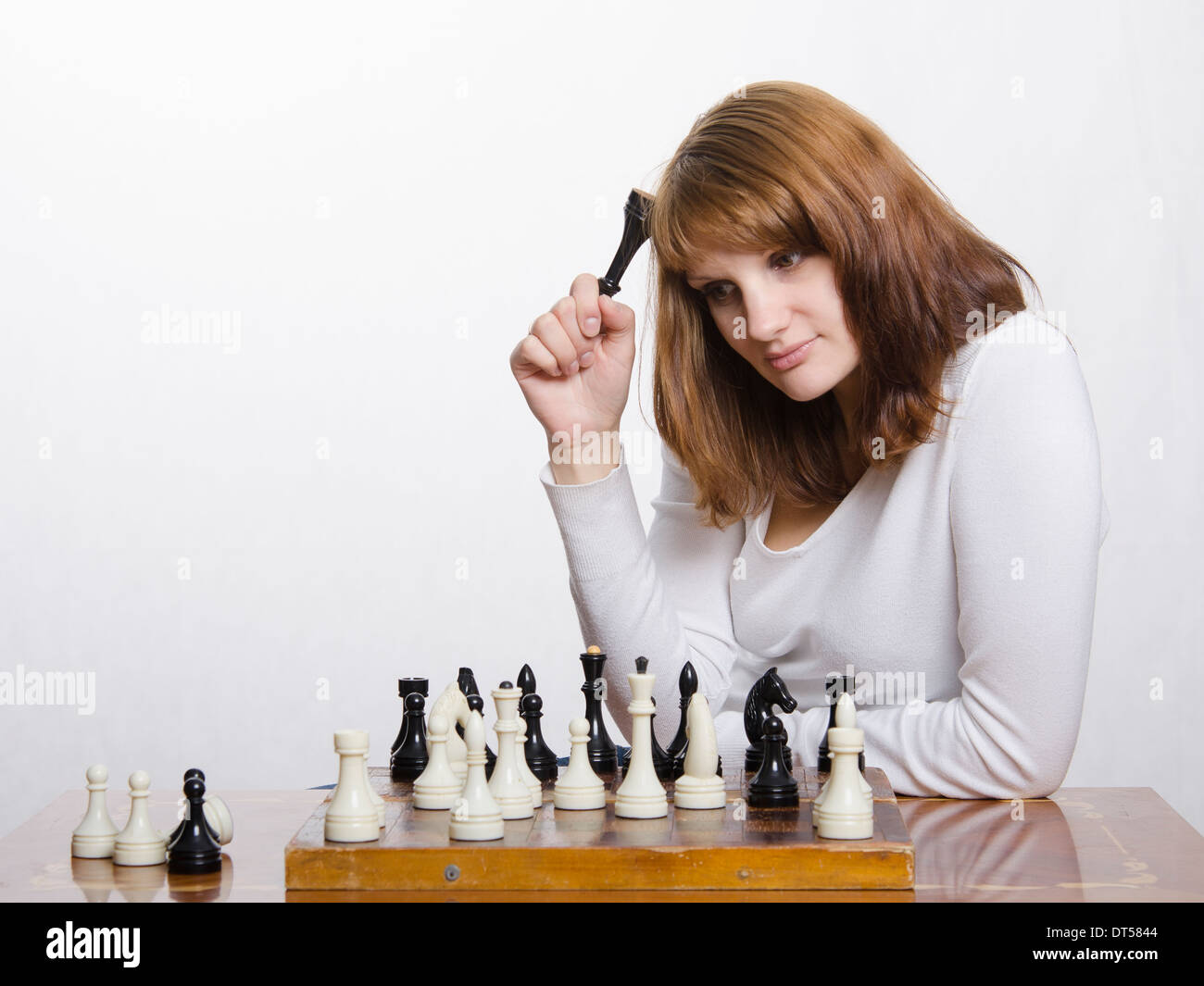 Young girl playing chess. A girl holds the shape of the Queen and ...