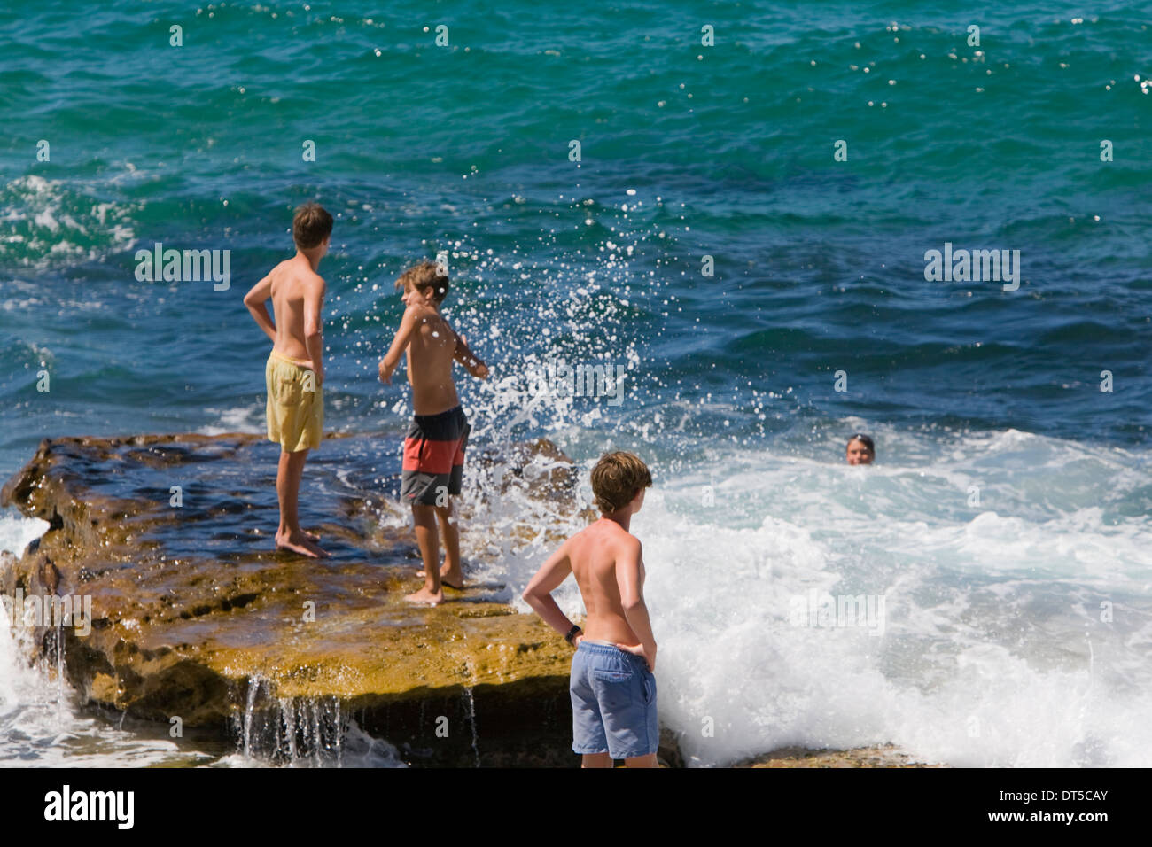 four young boys playing a game of jumping off the rocks into the surf ...