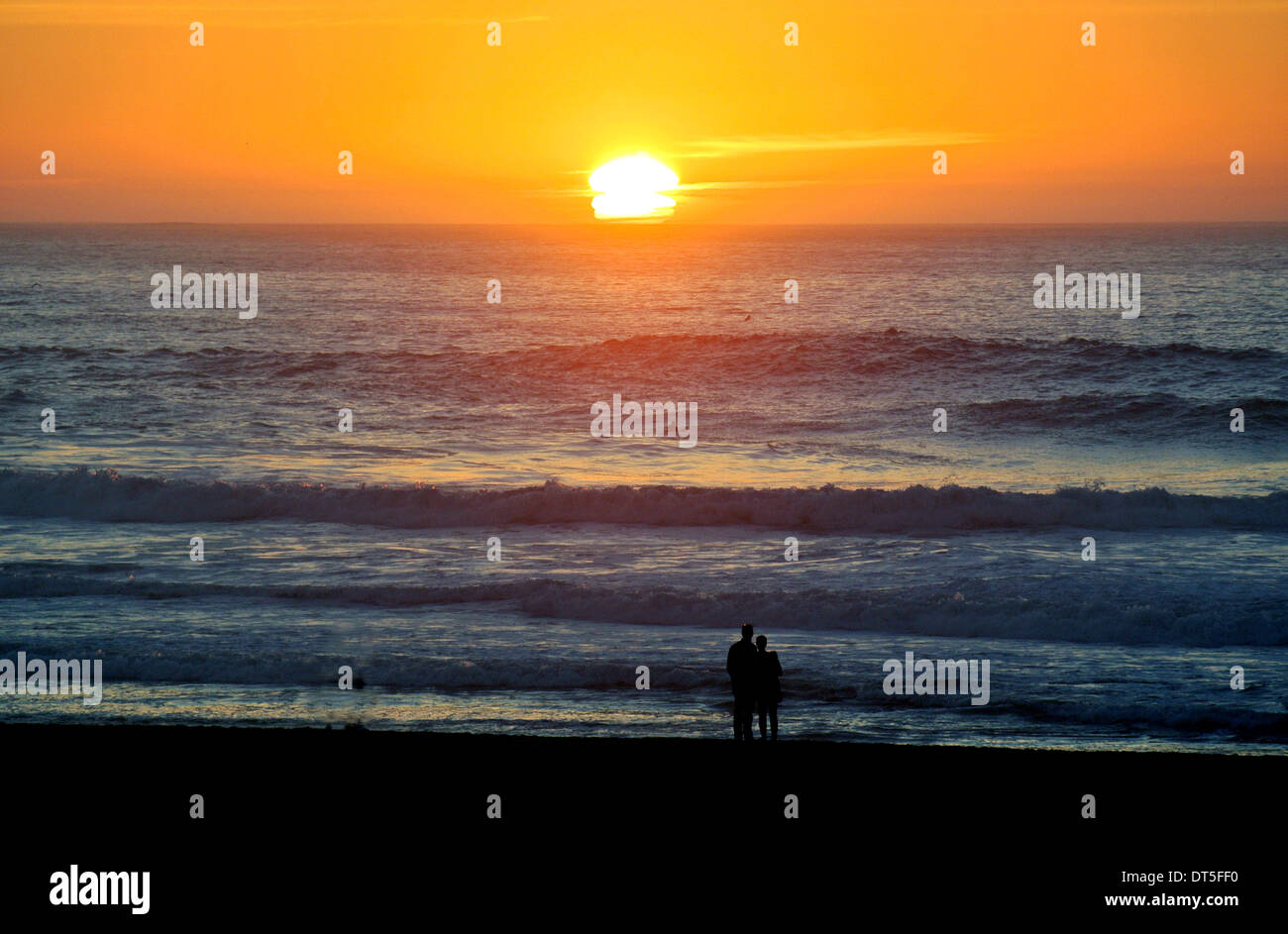 couple watch the sun set over pacific ocean at ocean beach in San ...