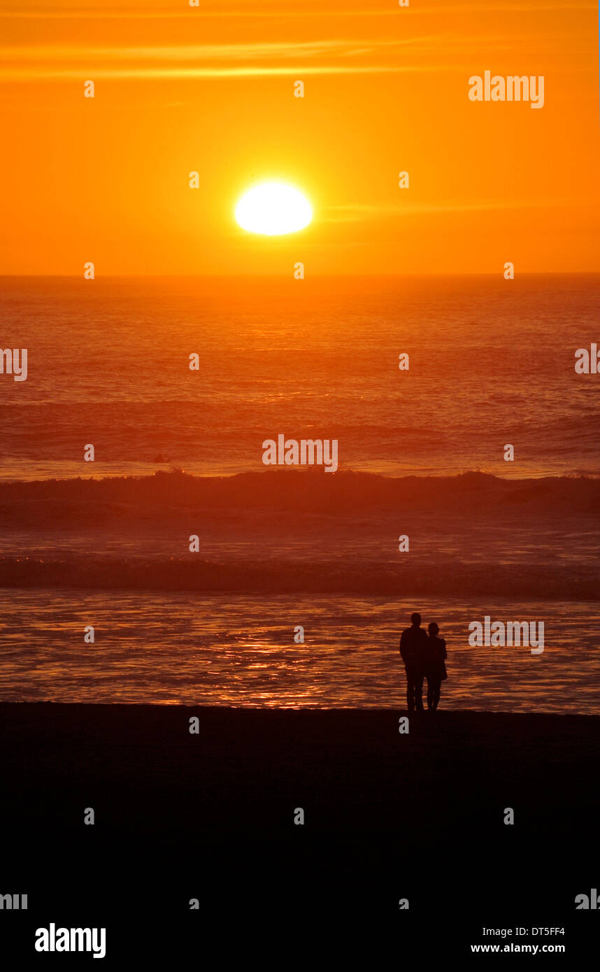 couple watch the sun set over crashing waves at ocean beach in san ...