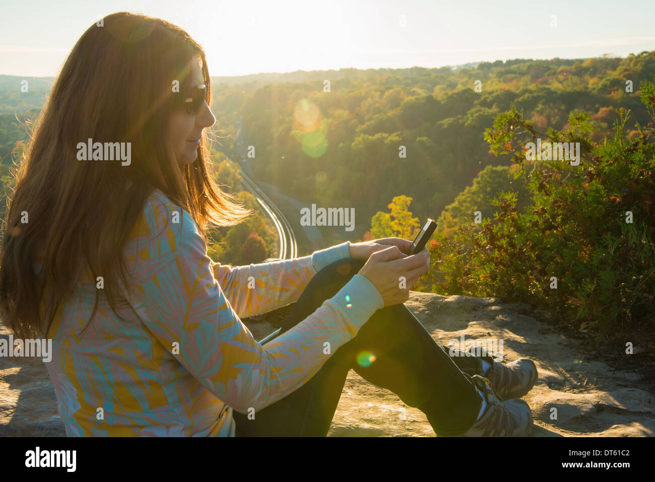 Mid adult woman sitting on elevated rock using mobile phone Stock Photo ...