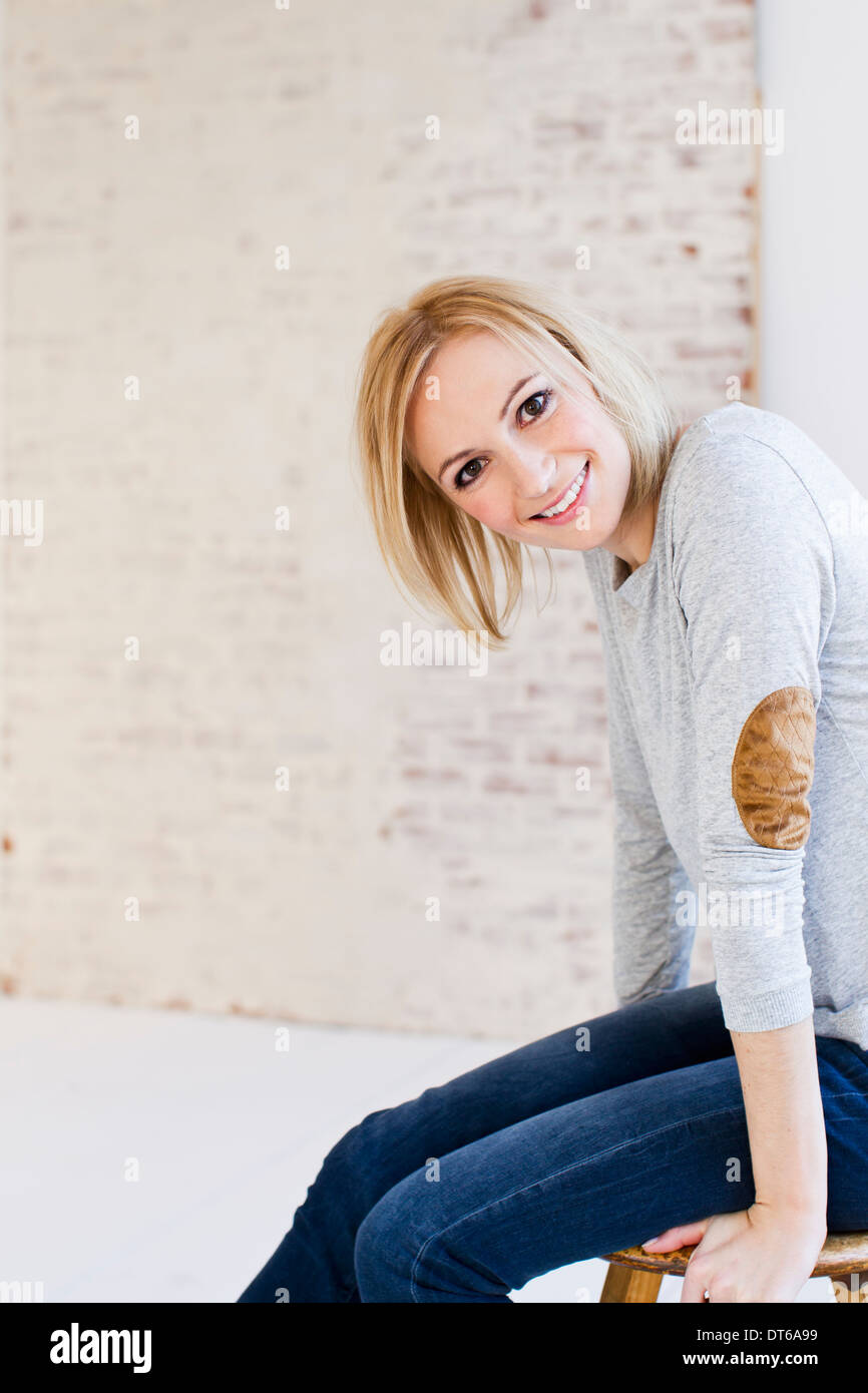 Studio portrait of young woman sitting on stool Stock Photo - Alamy