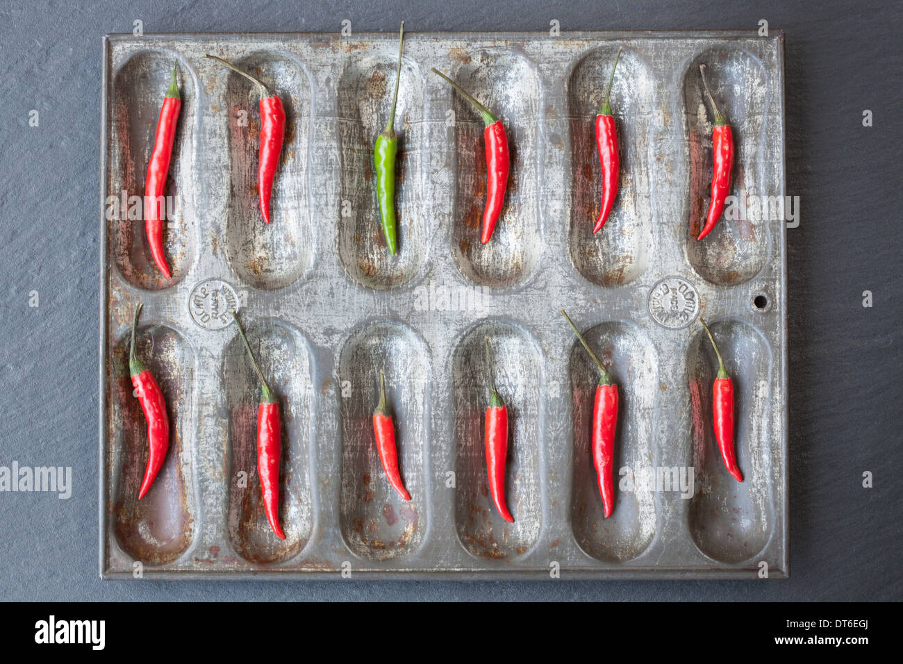 Large group of red chillies and one green chilli ordered in baking tin ...