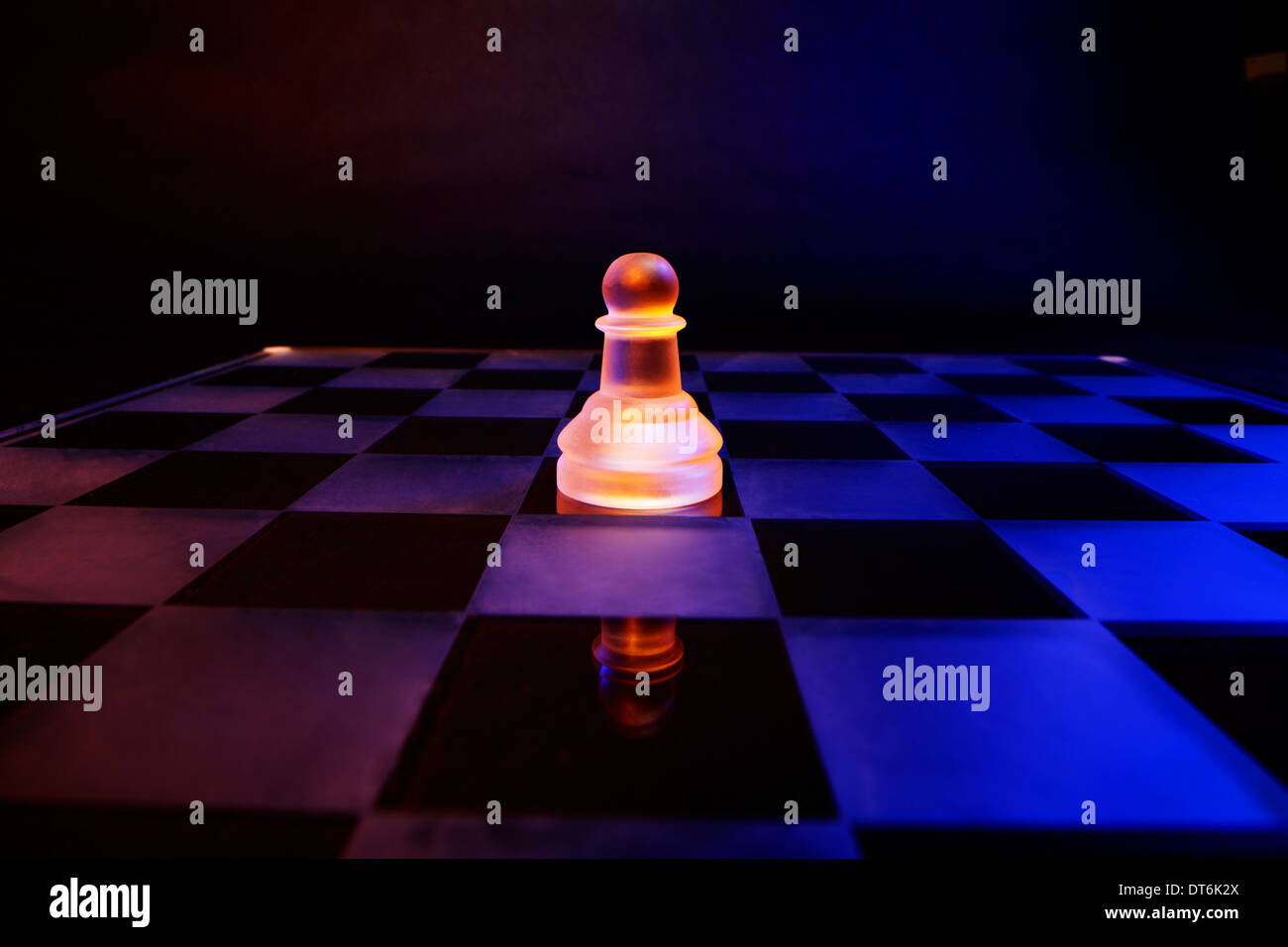 Glass chess on a chessboard lit by a colorful blue and orange light and ...