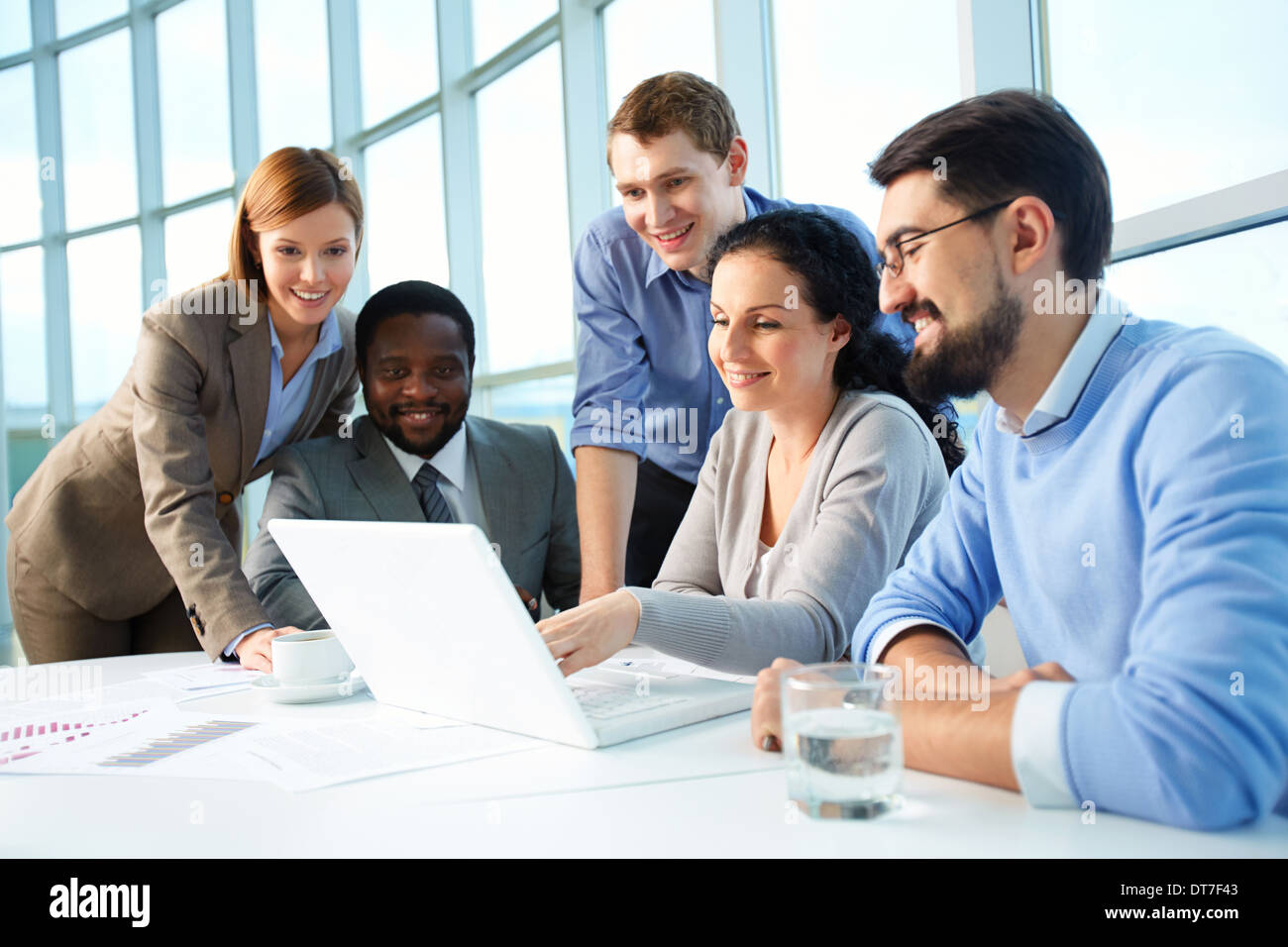 Group of business partners looking with smiles at laptop display at ...