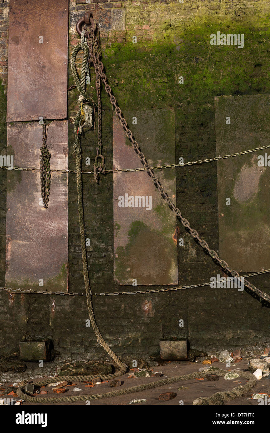 An old wall on the Thames foreshore with hanging chains and rope Stock ...
