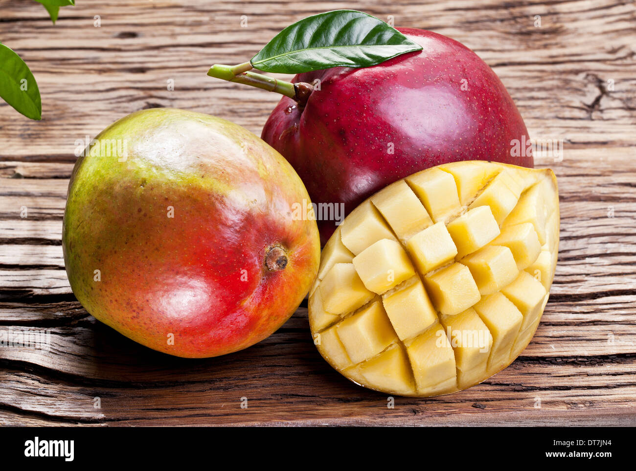 Mango fruits on a wooden table with green foliage on the background ...