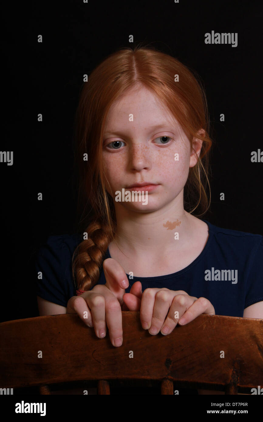 A beautiful red-headed child with her hair in a plait stares away from ...