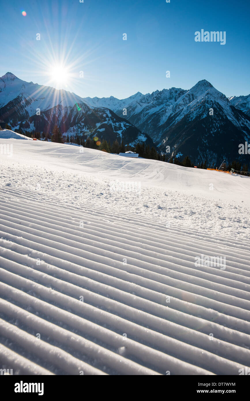 The sun shines over a fresh prepaired slope on a mountain at the ski ...