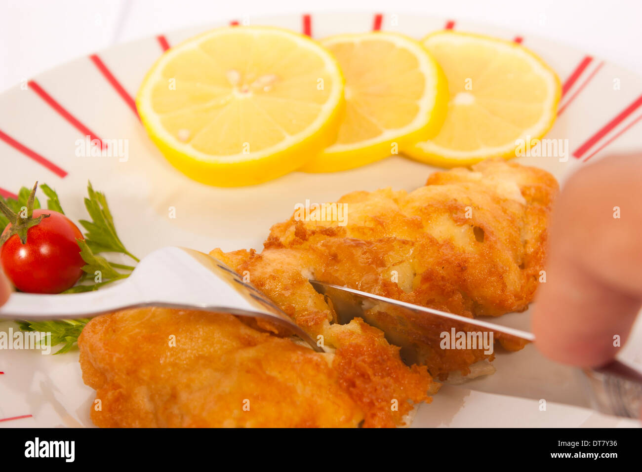 Fish schnitzel and lemon with a hand cutting the fish schnitzel on a ...