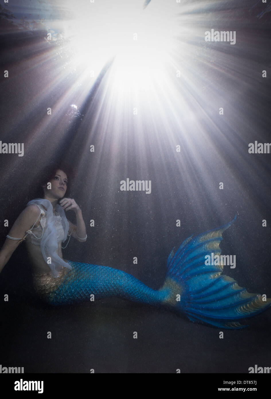 Young mermaid being lit by a sun rays shining through the water's ...