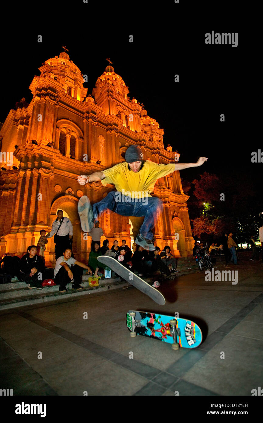 China, Beijing. Boy skateboarding in St Josephs Square in front of the ...