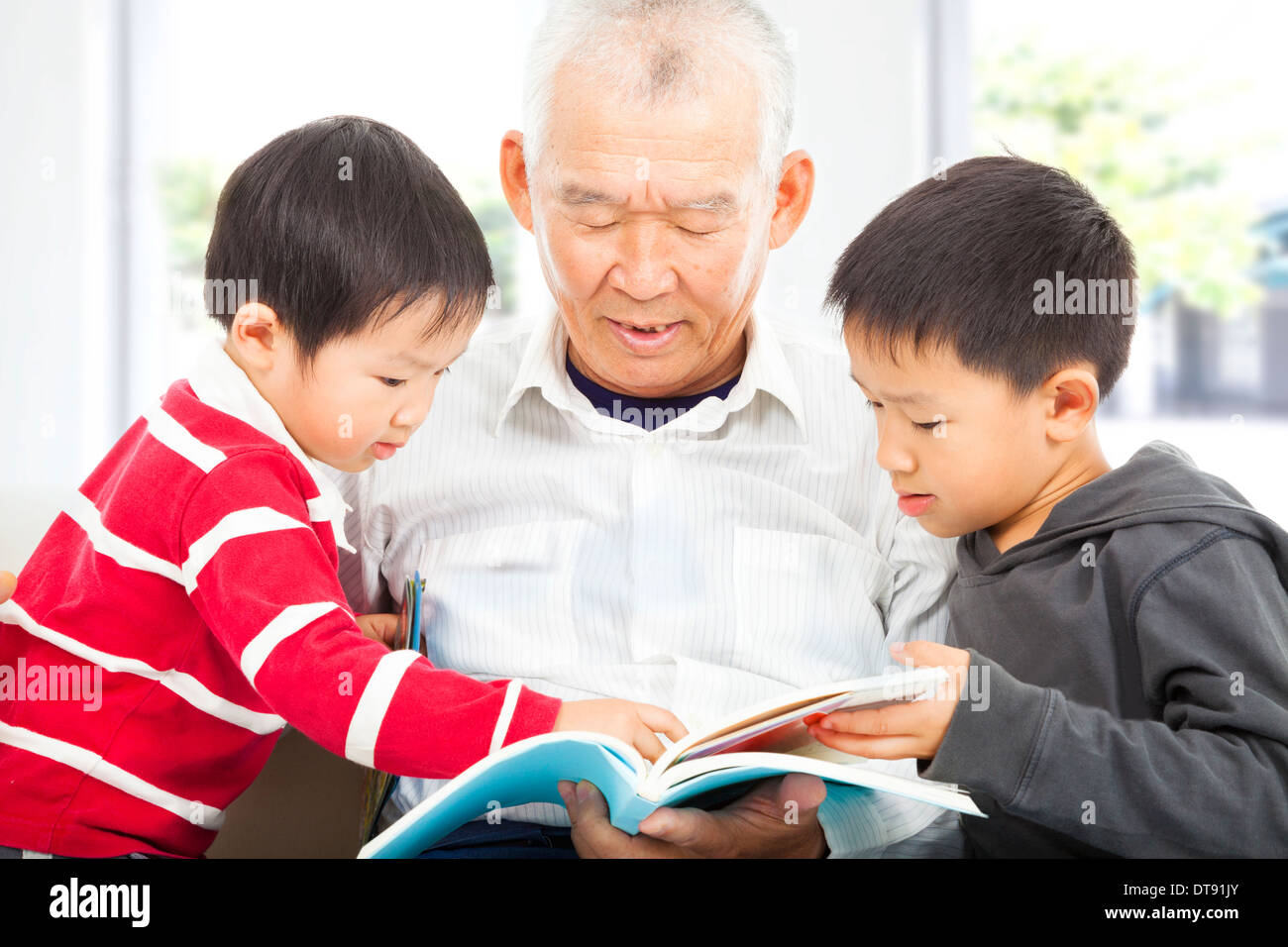 grandfather and grandchildren reading a book at home Stock Photo - Alamy