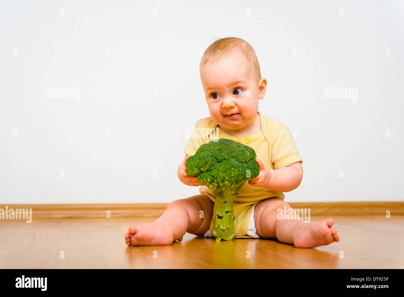 Cute baby eating broccoli at home - unhappy expression Stock Photo - Alamy