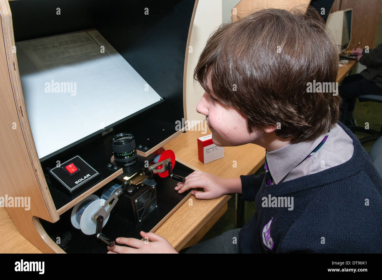 A schoolboy in uniform concentrates using a microfiche reader in an ...