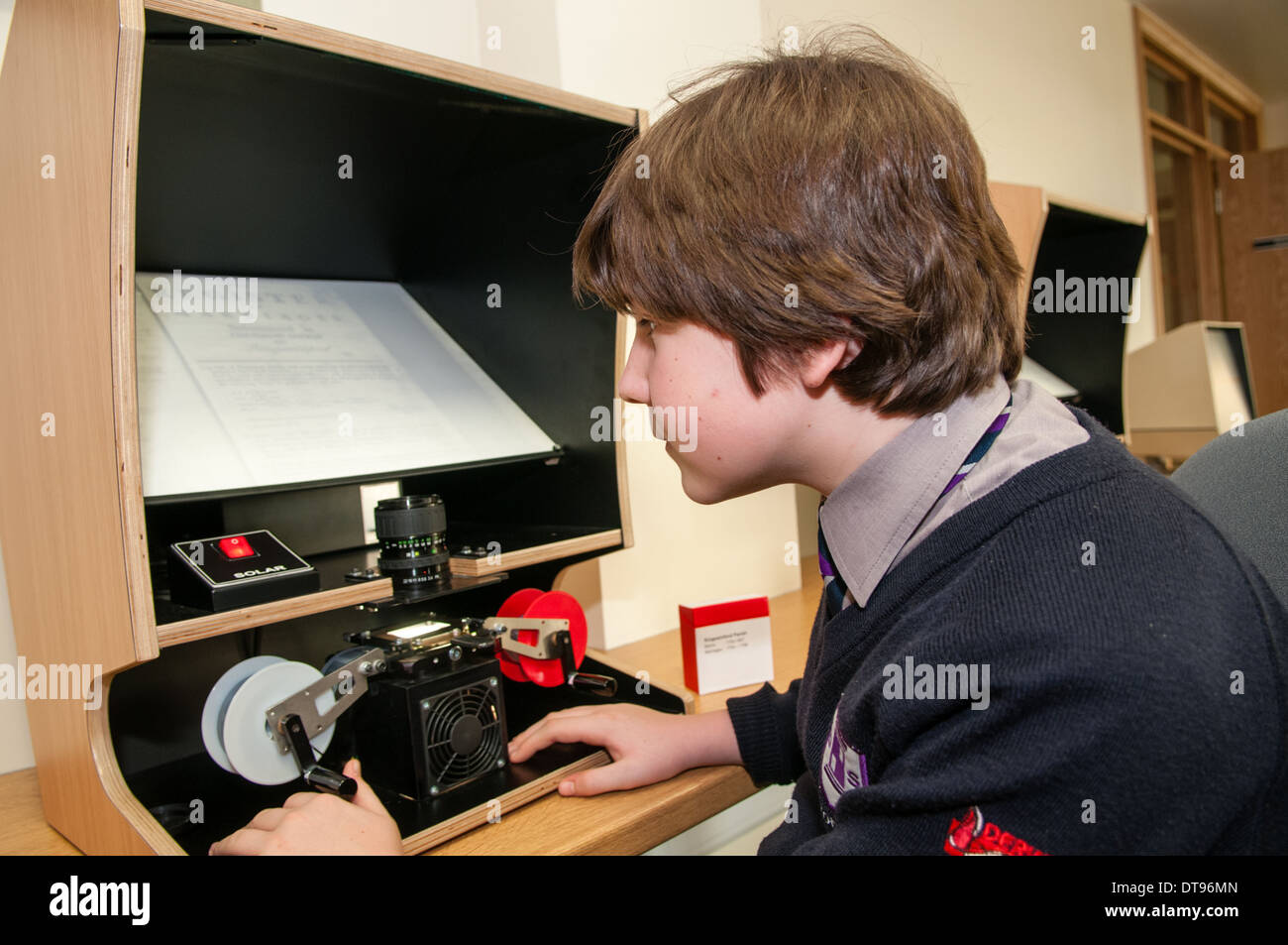 A schoolboy in uniform concentrates using a microfiche reader in an ...