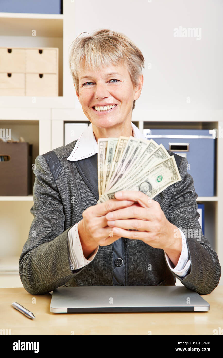 Elderly happy business woman with fan of dollar bills in the office ...