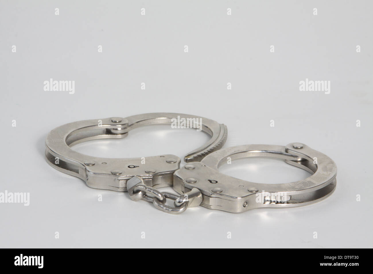 Metal handcuffs on a light coloured background Stock Photo - Alamy