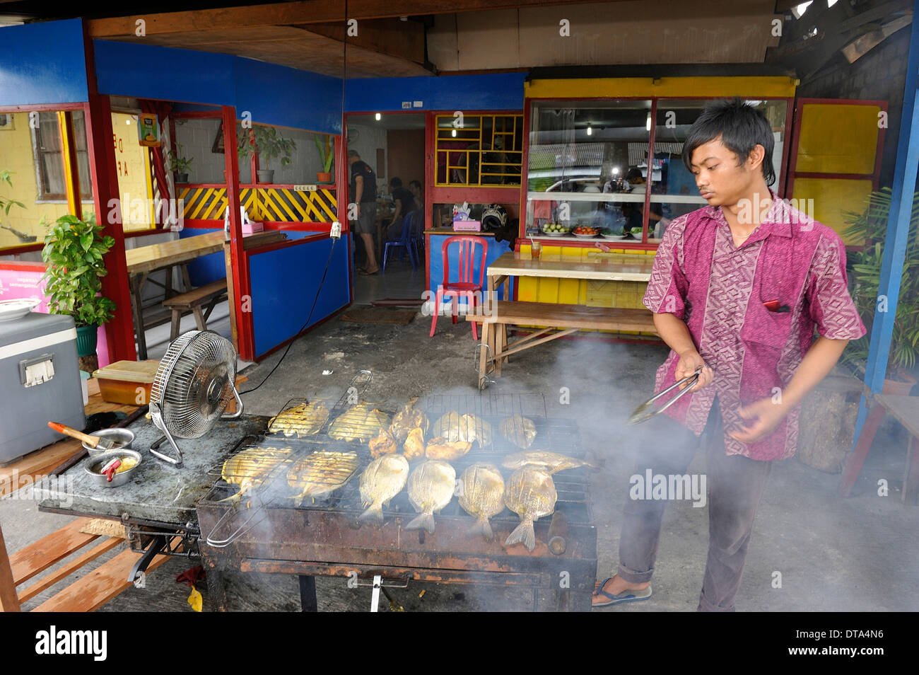 Javanese man grilling fish in a restaurant, Biak city, Biak Island ...
