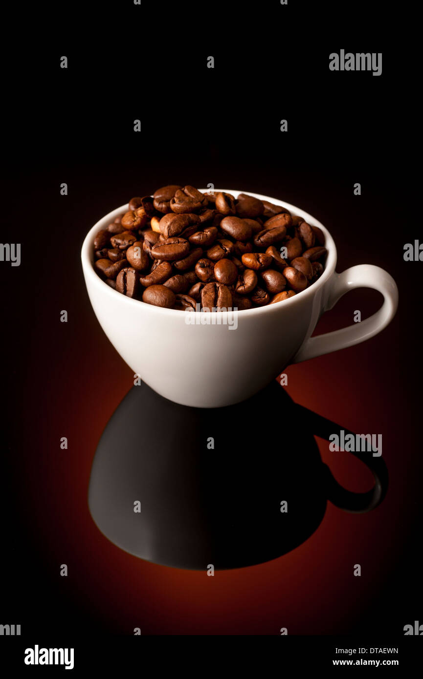 Dark roast espresso coffee beans in small espresso cup on reflective ...