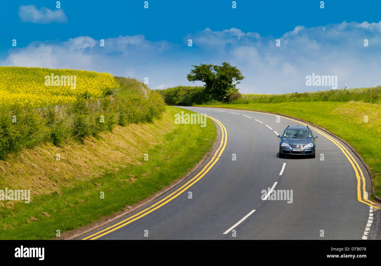 Bend on country road with blue sky and tree in background and car ...