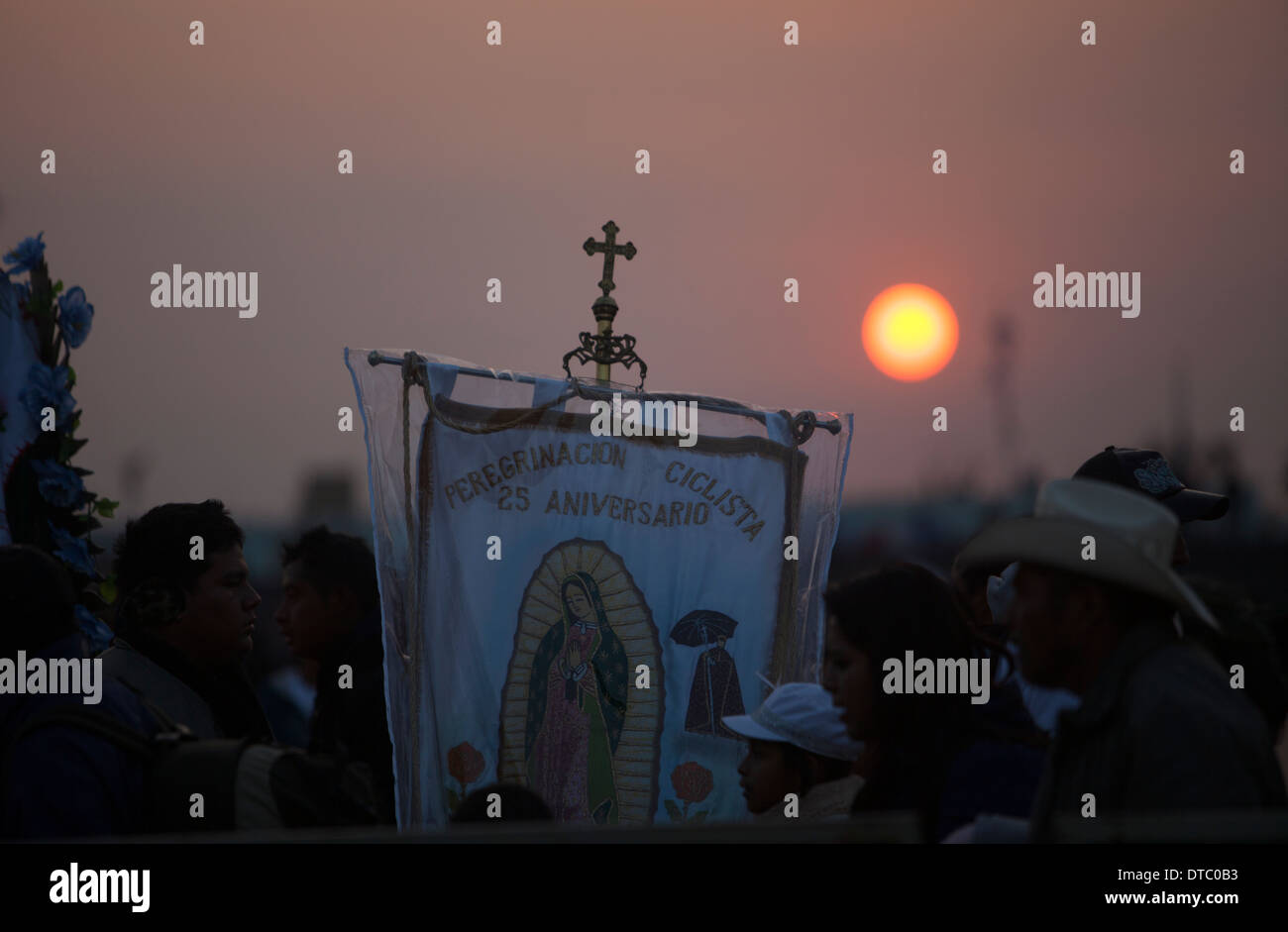 A pilgrim holds an banner of the Virgin of Guadalupe as the sun rises ...