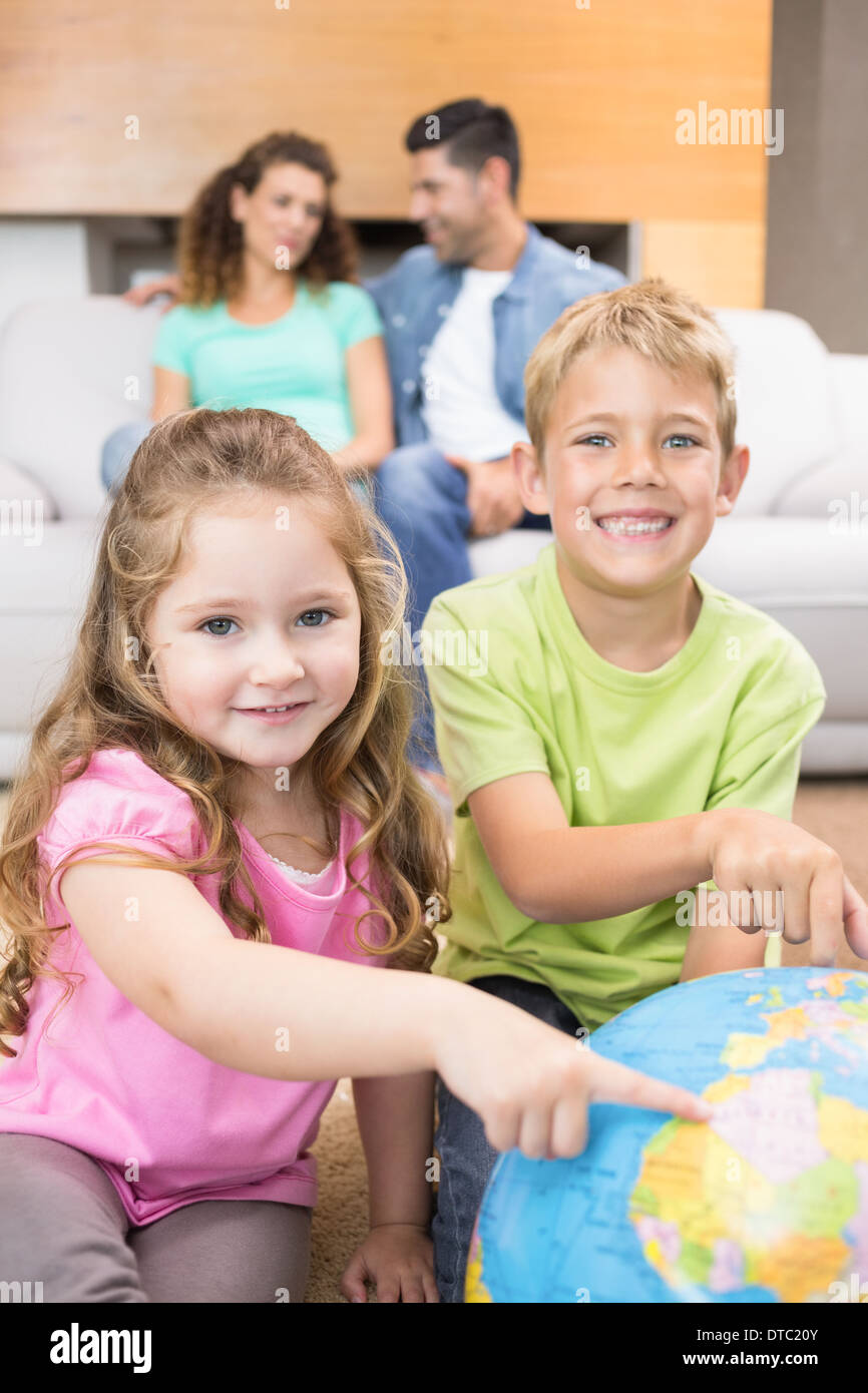 Smiling siblings pointing to globe on the rug Stock Photo - Alamy