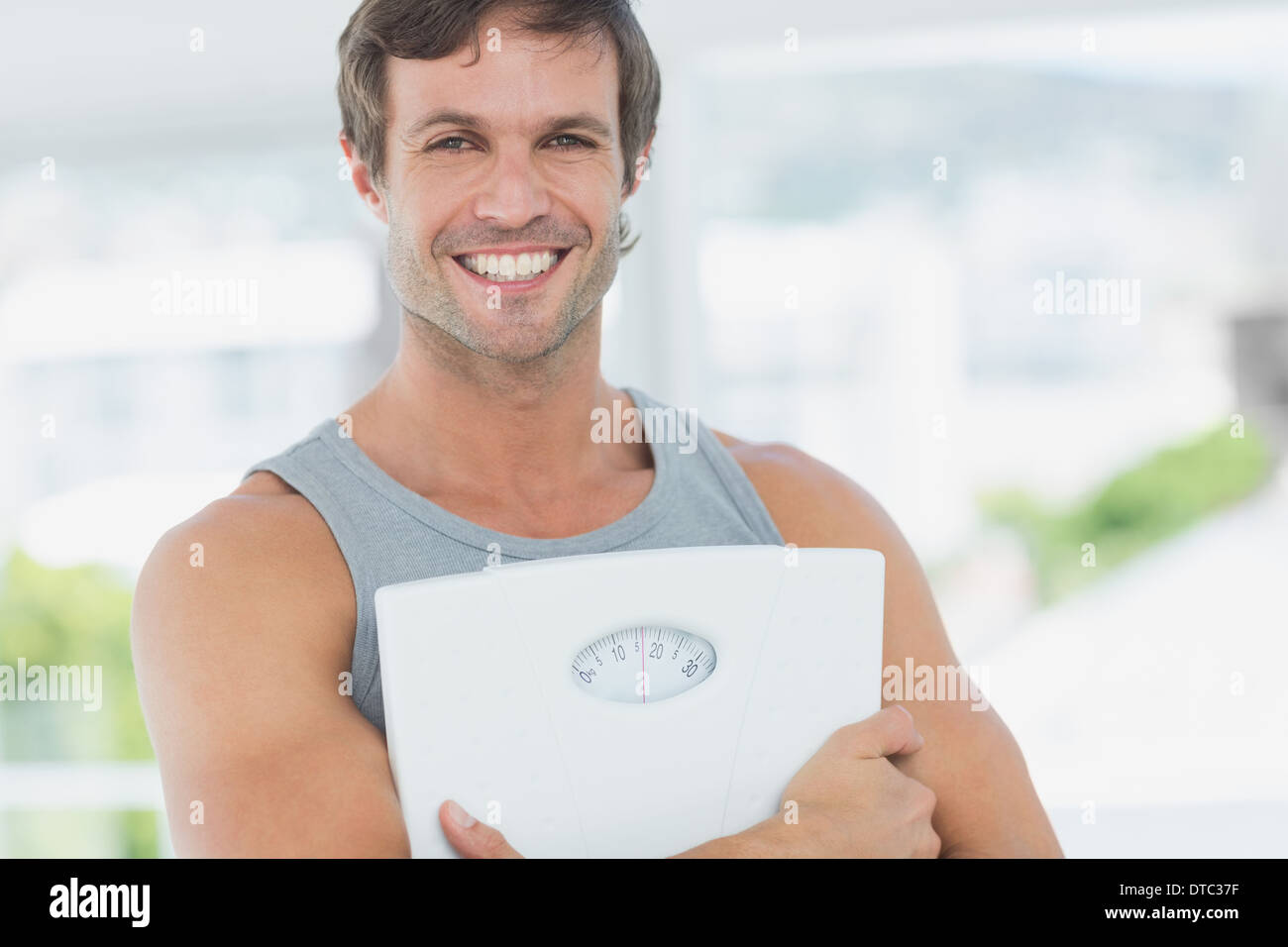 Fit young man with scale in bright exercise room Stock Photo - Alamy