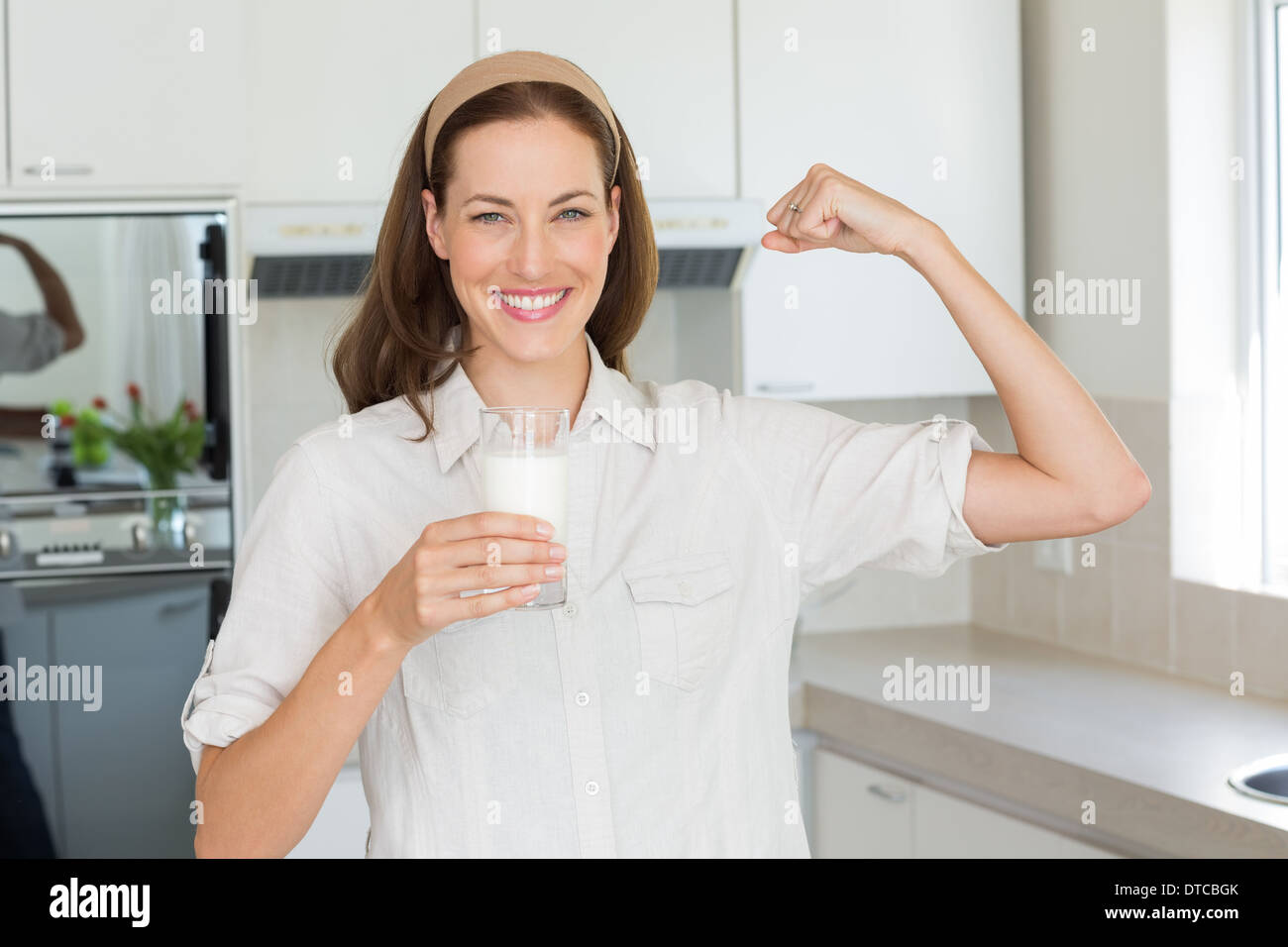 Happy woman flexing muscles while drinking water in kitchen Stock Photo ...