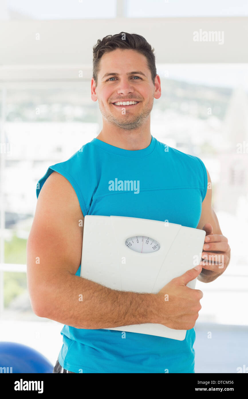 Sporty young man with weighing scale in gym Stock Photo - Alamy