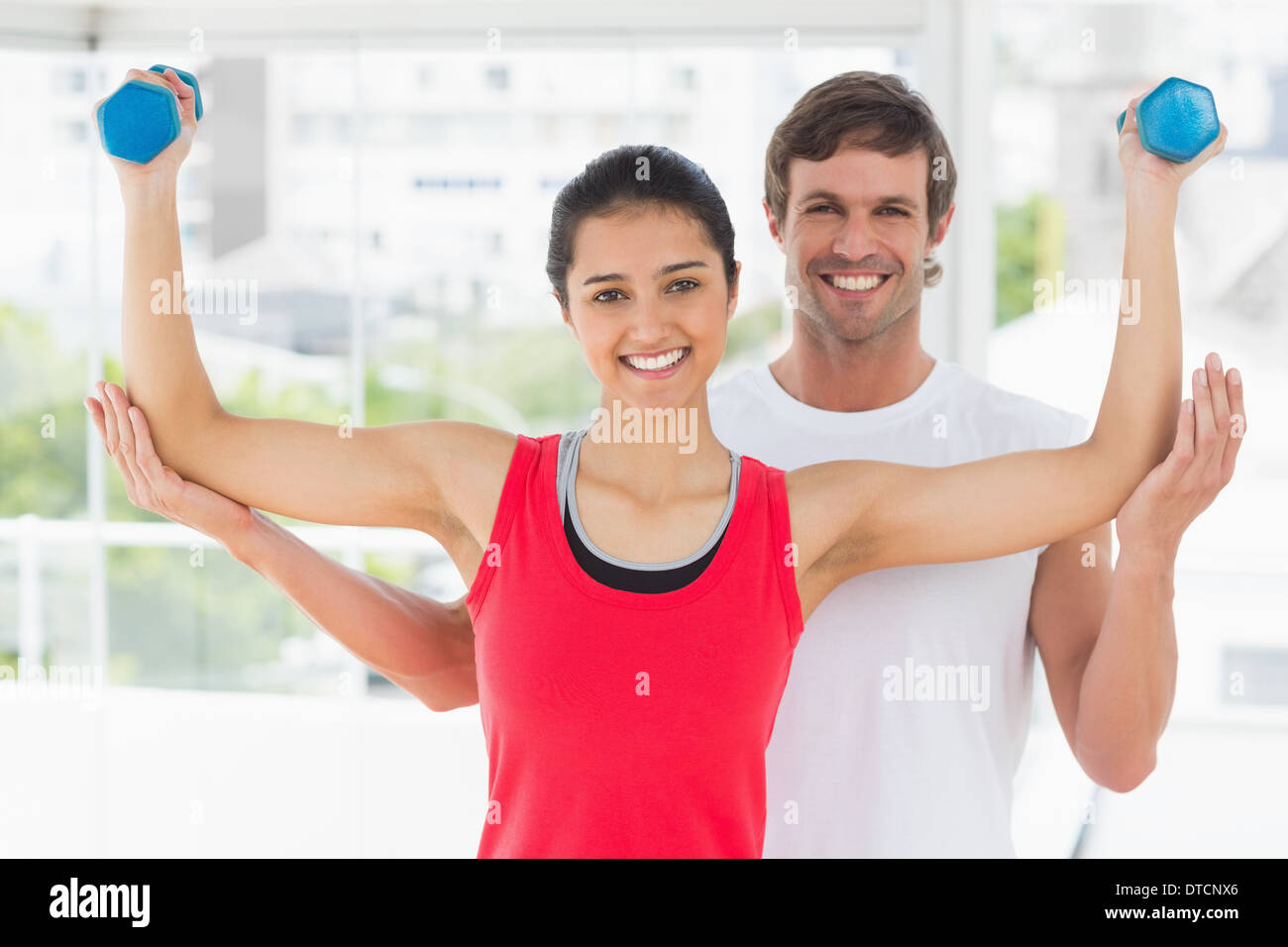 Smiling instructor with woman lifting dumbbell weights Stock Photo - Alamy