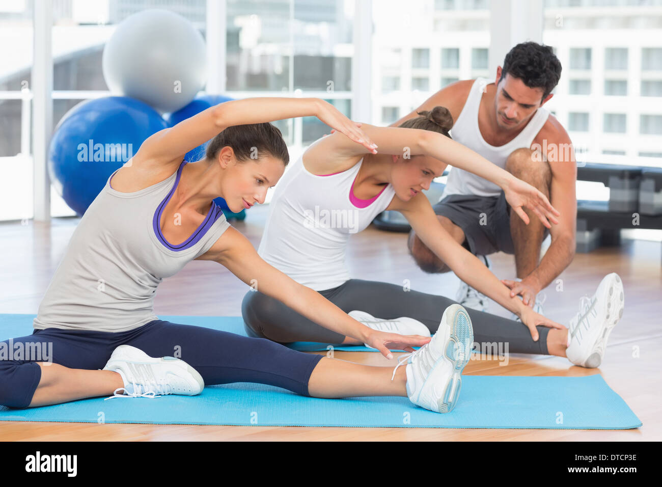 Women doing stretching exercises as trainer helps one Stock Photo - Alamy