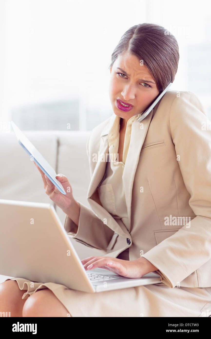Busy and stressed businesswoman sitting on sofa multi tasking Stock ...