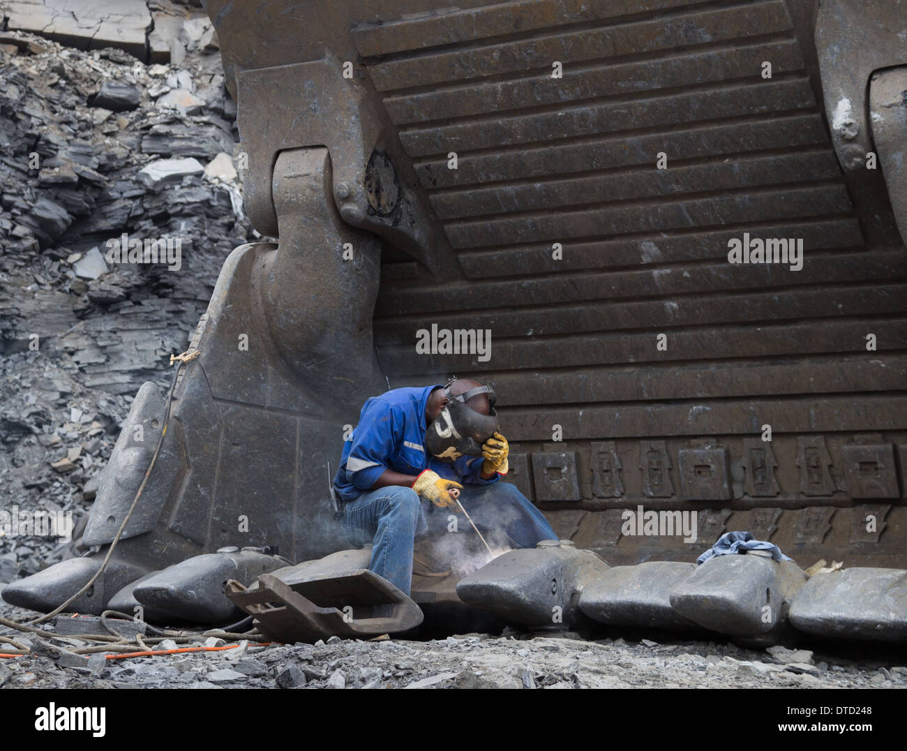 Worker welds repairs to a massive excavator/ digger bucket in a large ...