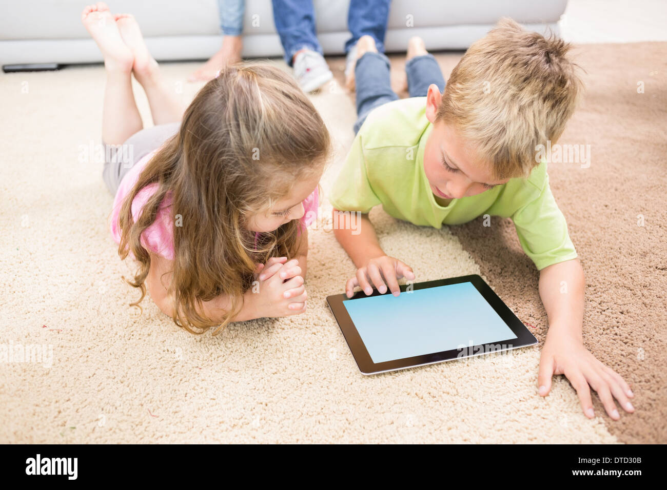 Smiling siblings lying on the rug using a tablet Stock Photo - Alamy