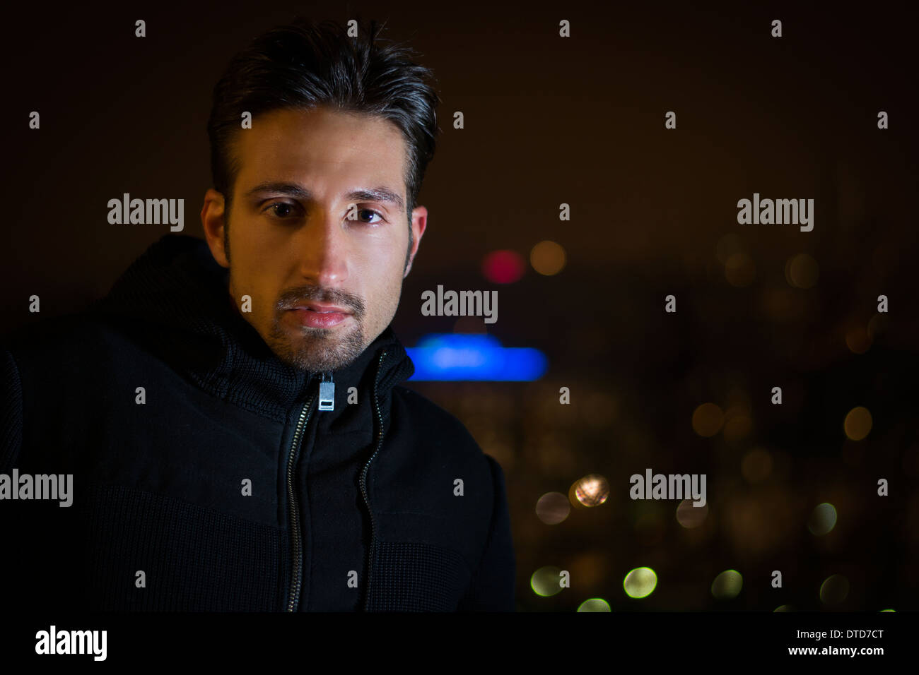 Attractive young man portrait at night with city lights behind him ...