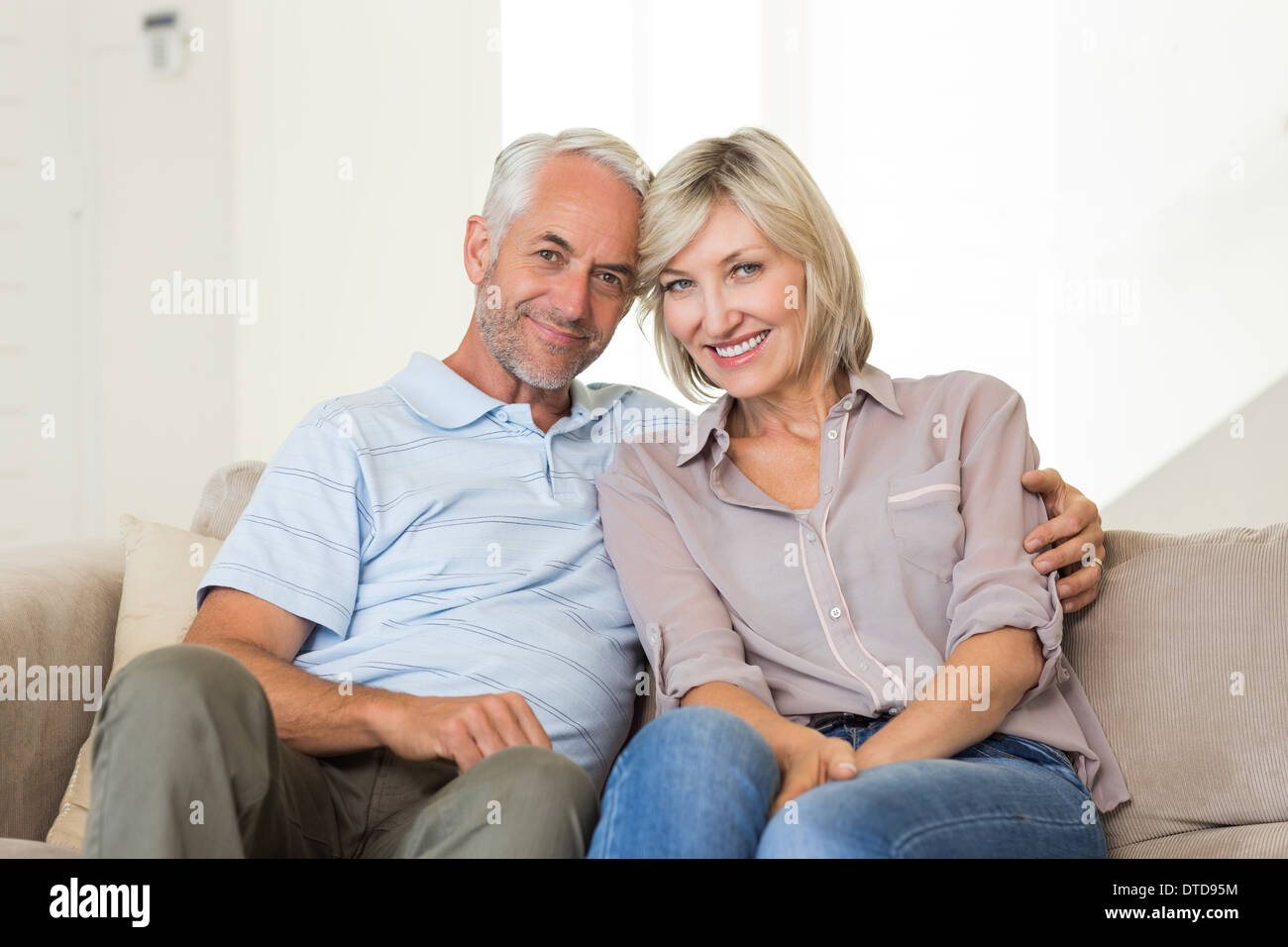 Smiling mature couple sitting on sofa with arm around Stock Photo - Alamy