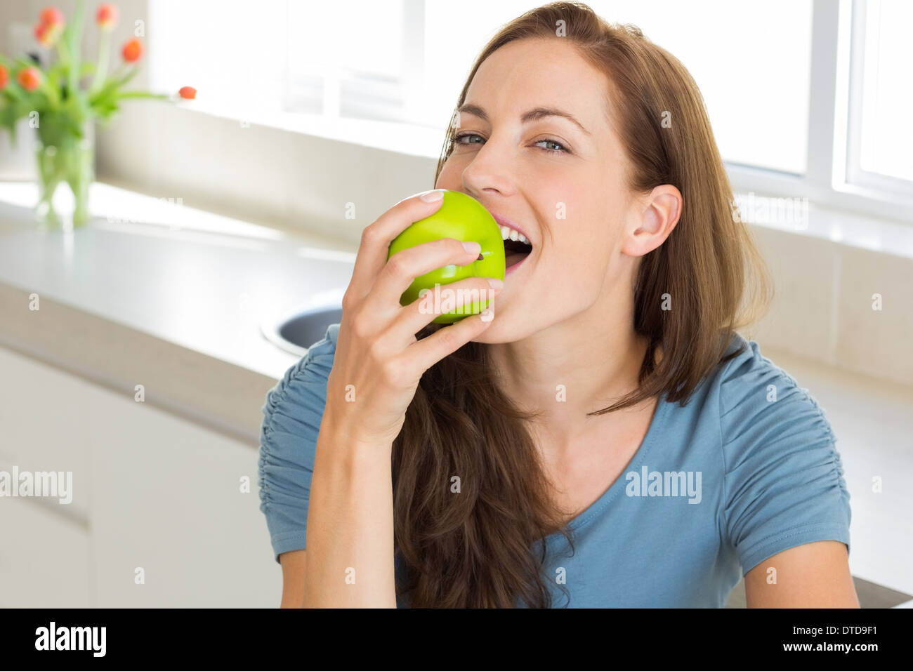 Smiling young woman eating apple in kitchen Stock Photo - Alamy