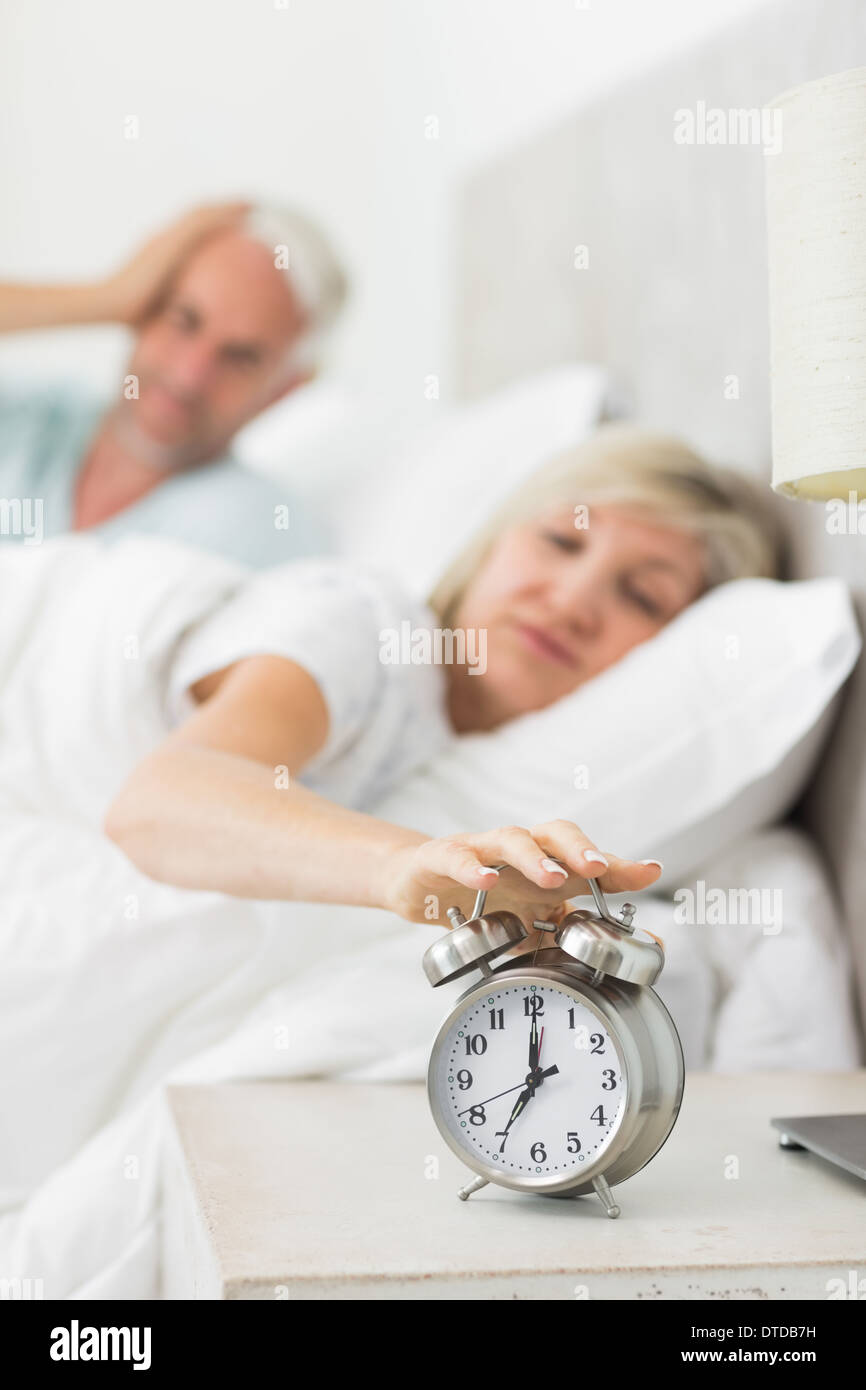 Mature woman extending hand to alarm clock in bed Stock Photo - Alamy