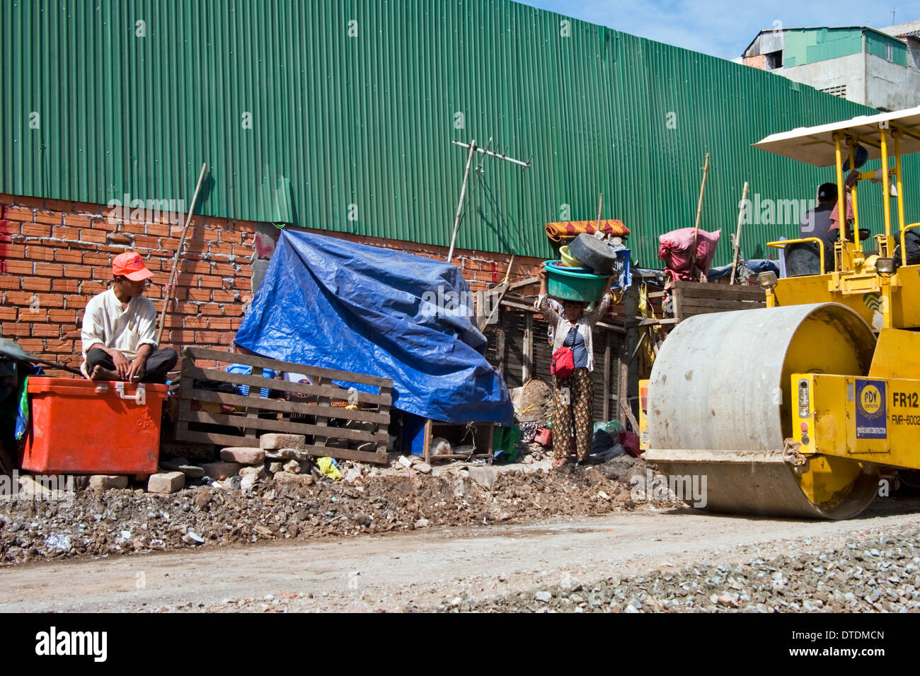 A man is sitting near a squatters home & posessions as a roller passes ...