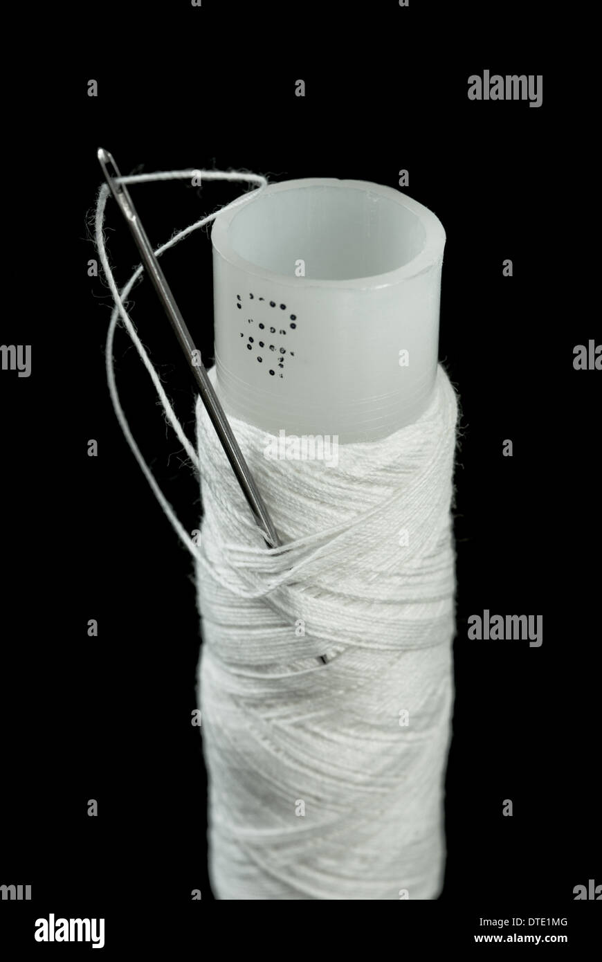 spool of white thread with a needle on a black background Stock Photo ...