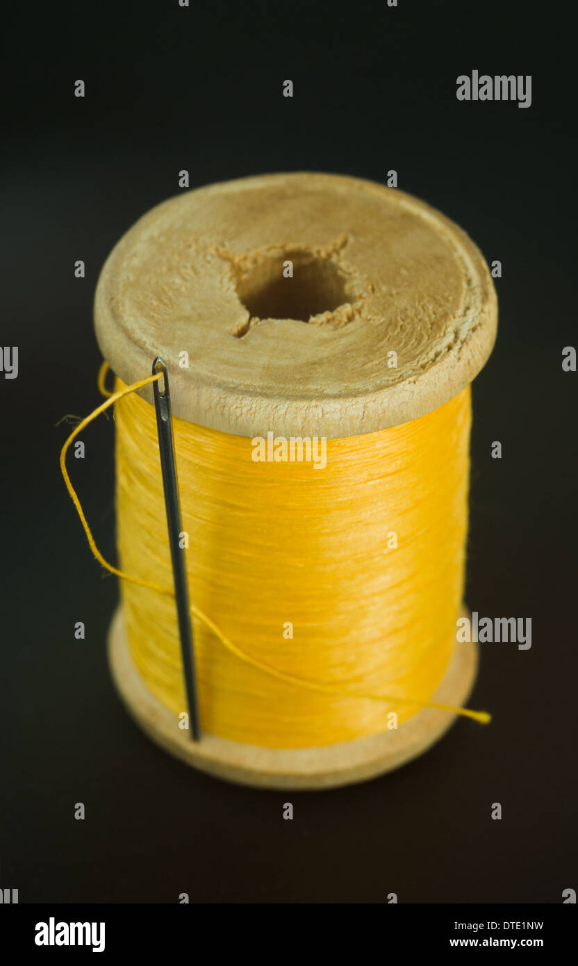 spool with yellow thread and needle on black background Stock Photo - Alamy