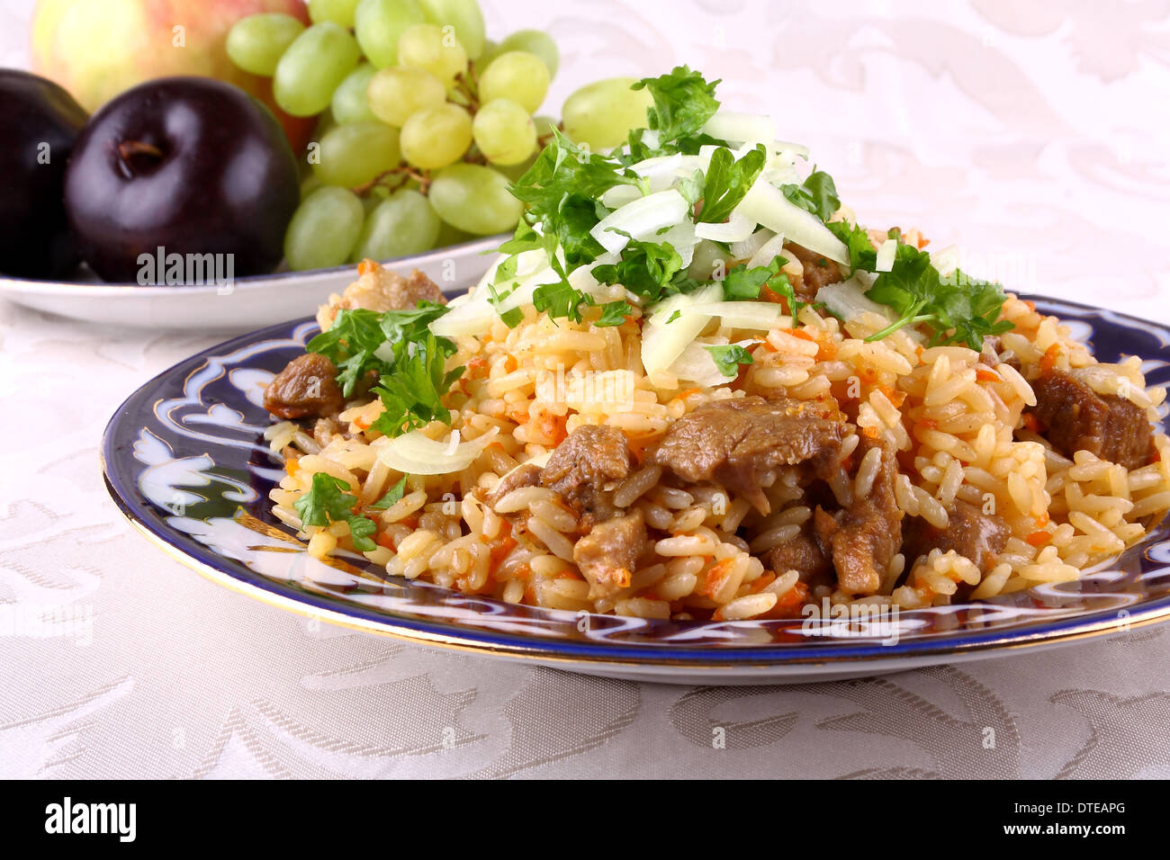 Uzbek pilaf in traditional dishes, fruits in background, horizontal ...