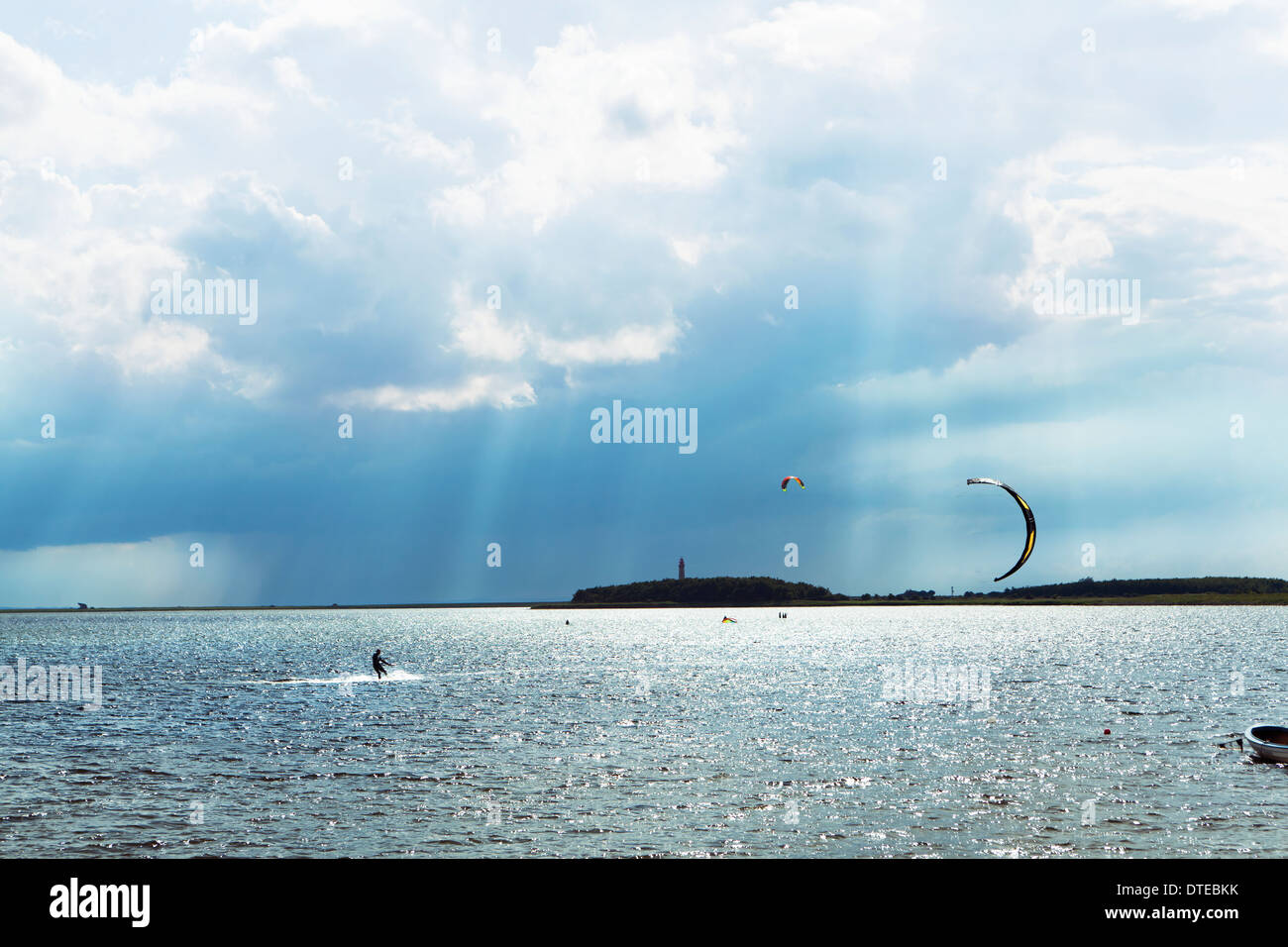 kitesurfer gliding over the water, sunbeam and dark sky Stock Photo - Alamy