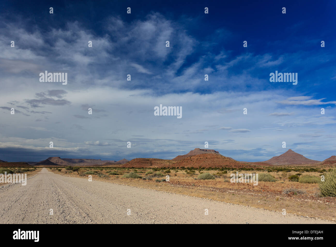 Shapely clouds in blue sky showcase sand dunes along long straight road ...