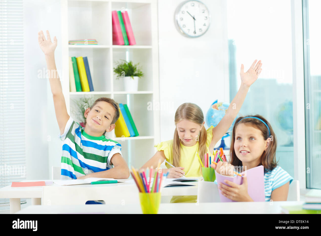 Portrait of clever schoolkids raising hands at workplace with their ... Portrait of clever schoolkids raising hands at workplace with their ...