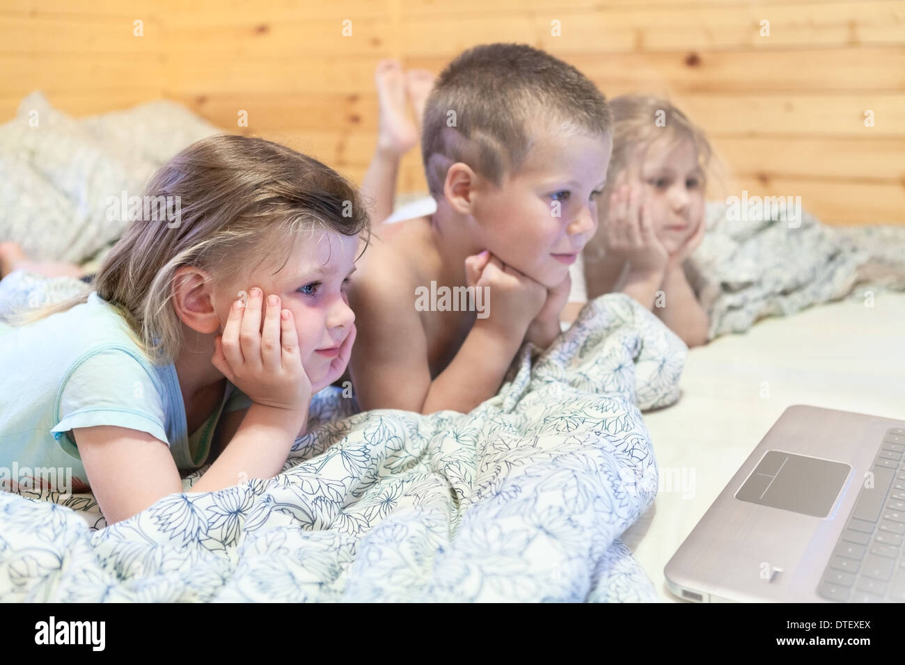 Lovely kids looking at computer monitor while laying in bed Stock Photo ...