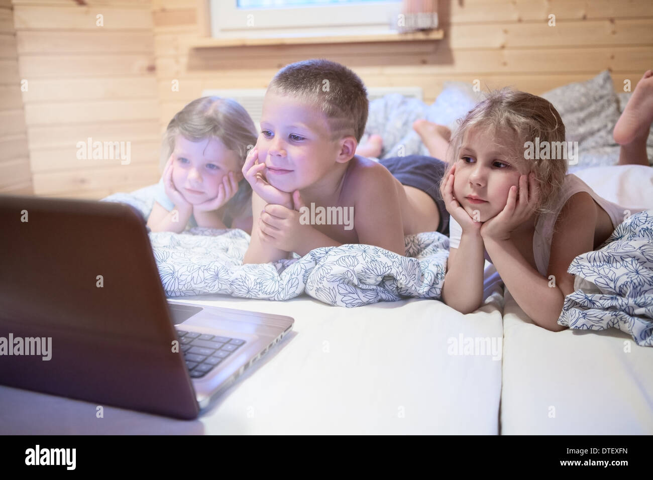 Three small children looking at laptop screen in bed Stock Photo - Alamy