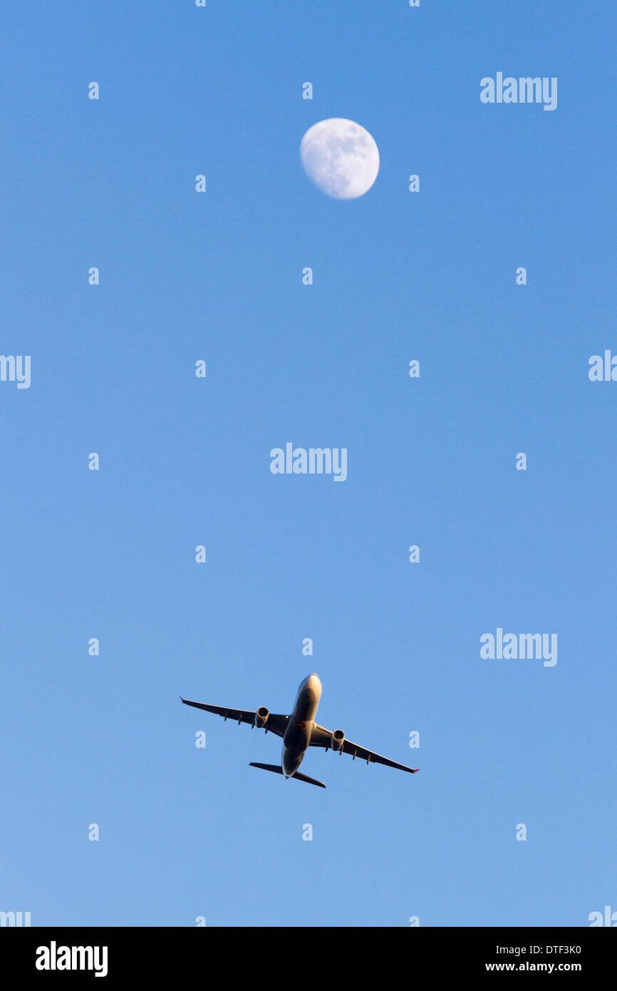 Plane flying across the sky with the moon in the background, England ...